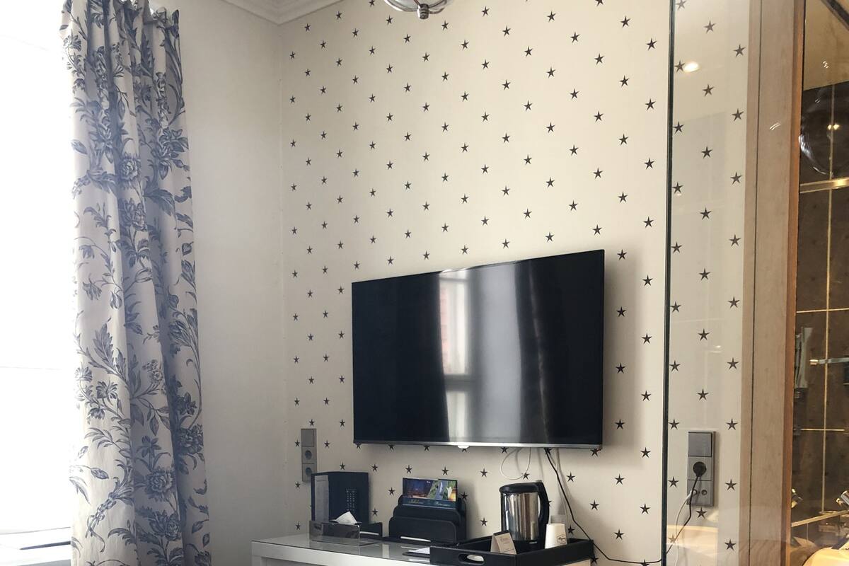 Quarto de hotel com cama, escrivaninha, televisão de tela plana, cafeteira e chuveiro.