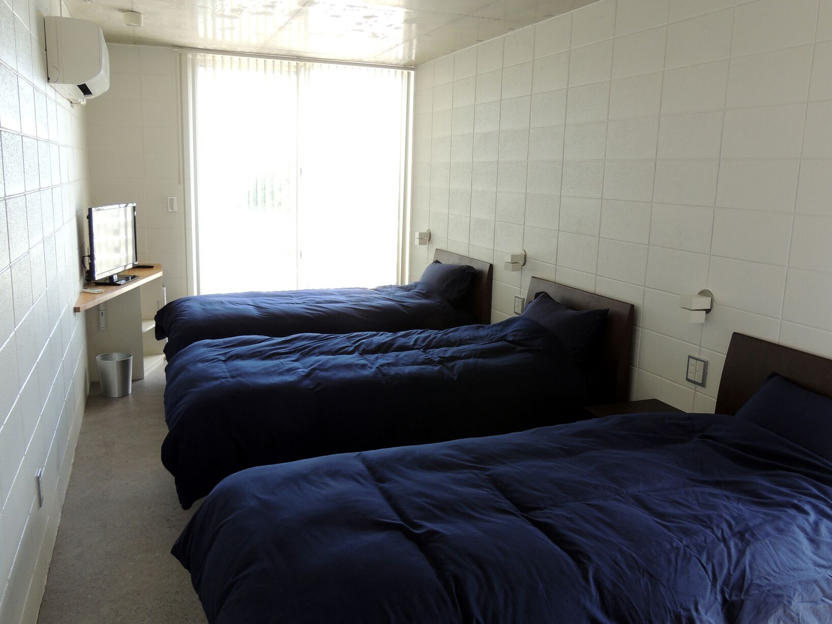 Quarto de hotel com duas camas, uma televisão em uma estante e uma janela com persianas.