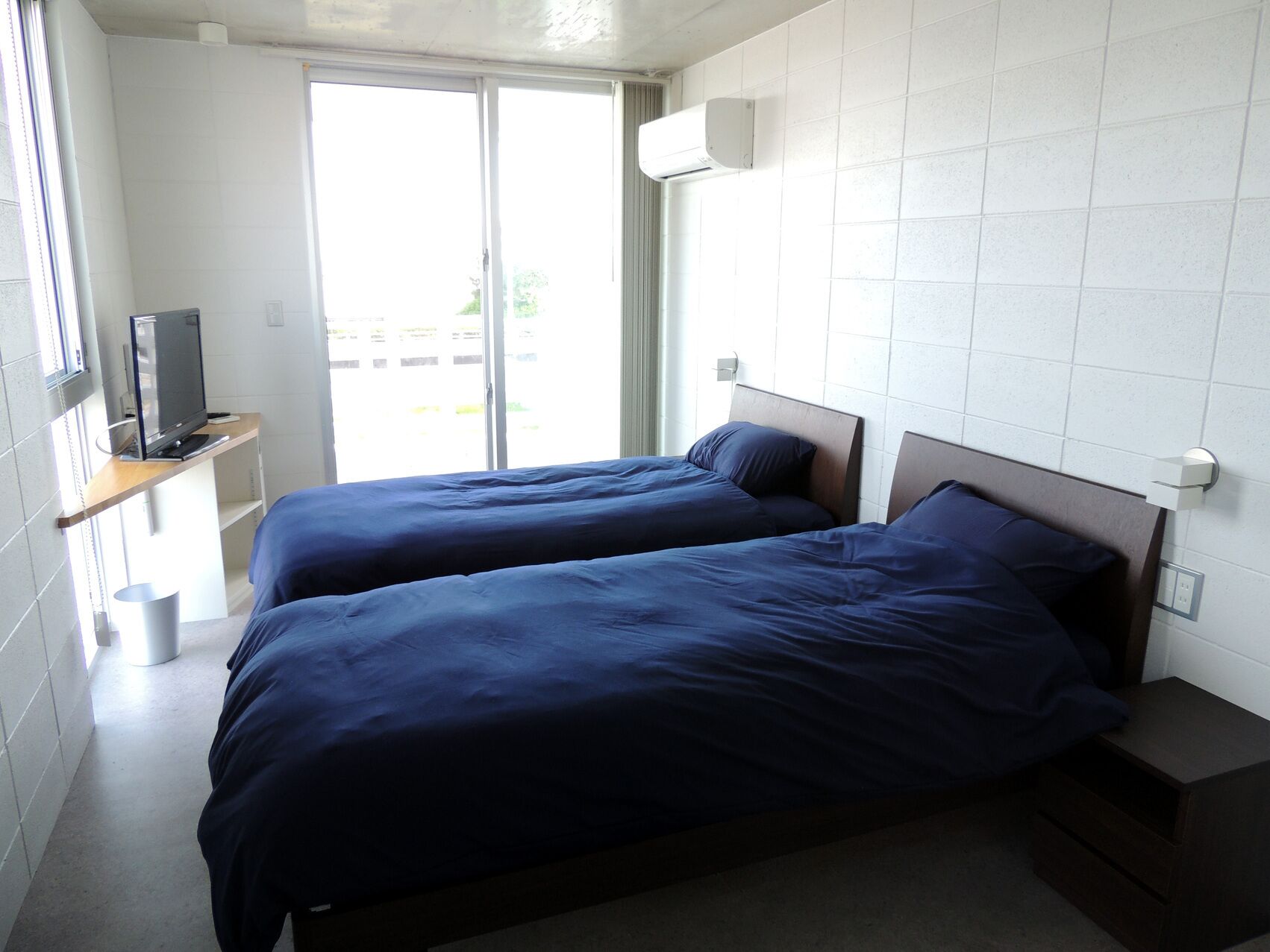 Quarto de hotel com duas camas, uma televisão em uma estante e uma porta de vidro deslizante para o exterior.