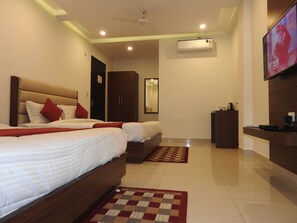 Quarto de hotel com duas camas, televisão, ventoinha no teto e ar condicionado.