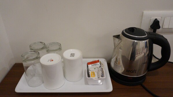 Uma mesa com uma cafeteira, um tabuleiro com chávenas, copos e uma caixa de cápsulas de café.