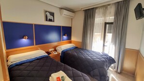 Quarto de hotel com duas camas, cabeceira de madeira, ar condicionado fixado na parede e janela com cortinas.