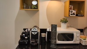 Uma área de cozinha com cafeteira, micro-ondas e uma prateleira com potes de vidro e uma planta em vaso.