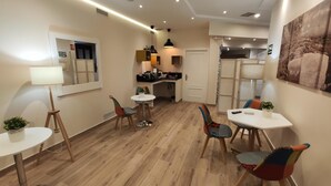 Um interior moderno com área de refeições, mesas redondas e cadeiras coloridas, cozinha com ilha central e uma grande pintura na parede.