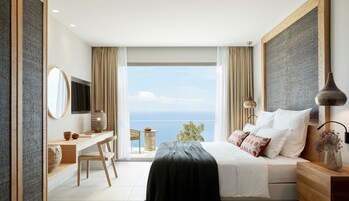 Quarto moderno com uma cama grande, uma escrivaninha e vista para o mar.