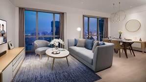 Sala de estar moderna com sofá, mesa de centro e área de jantar, com grandes janelas e vista para a cidade.