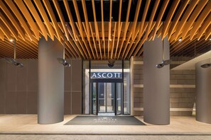 Uma entrada moderna com teto de ripas de madeira, porta de vidro e uma placa com o nome 'ASCOTT'.