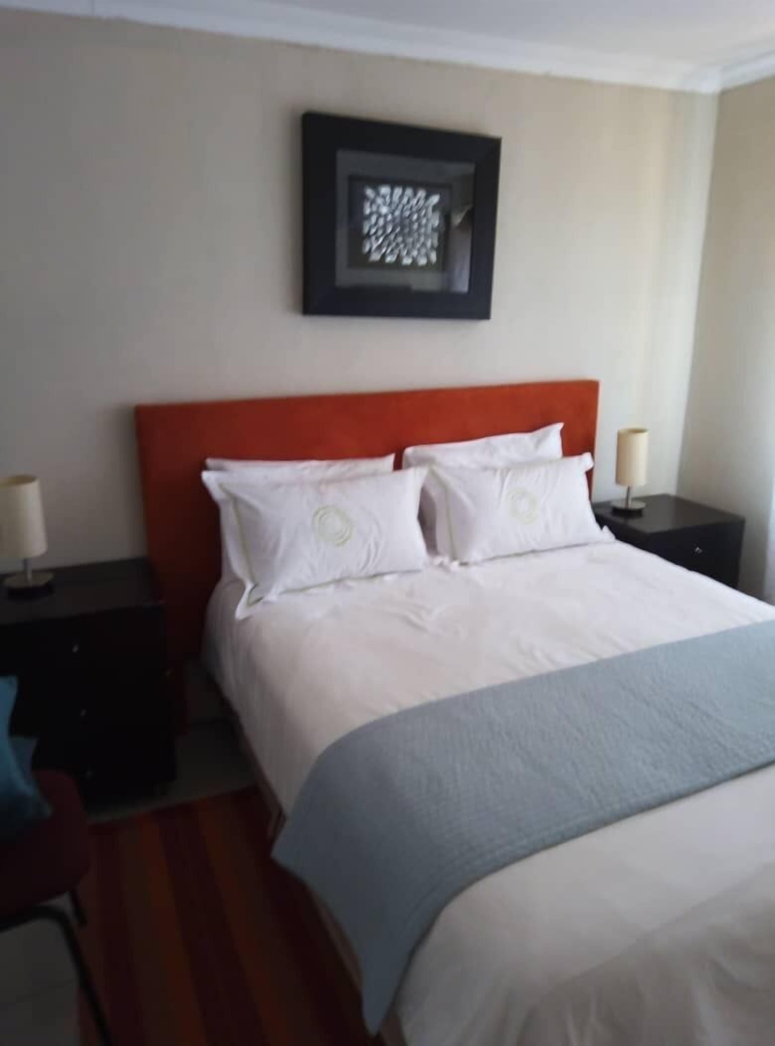 Quarto de hotel com uma cama, mesa de cabeceira, luminária e quadro na parede.