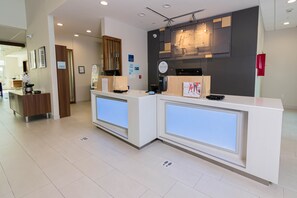 Uma área de recepção com design moderno, com um balcão de atendimento, um painel digital fixado na parede e um armário de madeira.