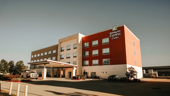 Edifício do Holiday Inn Express & Suites, com design moderno, apresentando uma combinação de cores vermelhas e bege, várias janelas e área de estacionamento coberta.