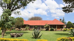 Um edifício de pedra com telhado vermelho, rodeado por jardins bem cuidados e diversas plantas.