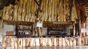 Um espaço de bar rústico com ripas de madeira e prateleiras exibindo garrafas e petiscos.