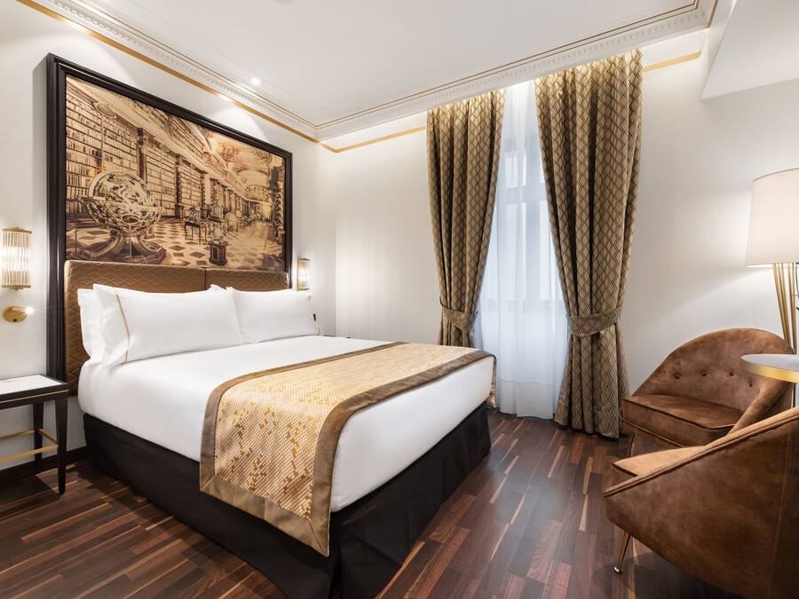 Quarto de hotel com uma cama grande, uma mesinha de apoio, uma cadeira, uma escrivaninha e um quadro grande na parede.