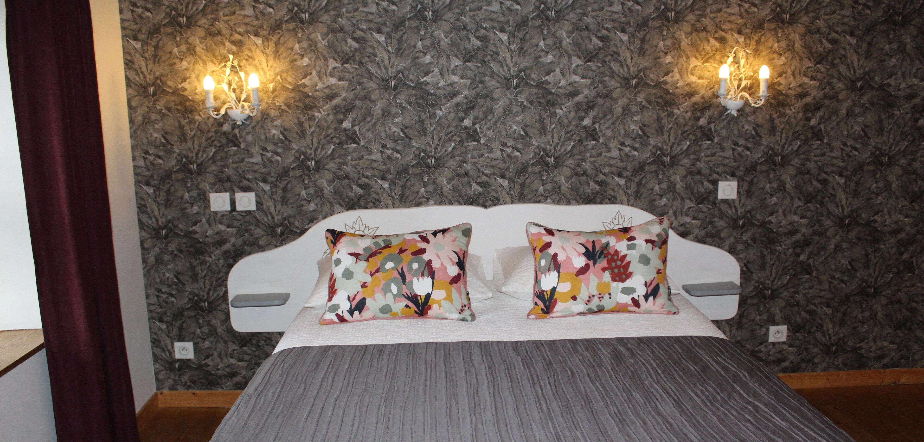 Quarto com uma cama, duas luminárias na parede e um papel de parede estampado com flores.