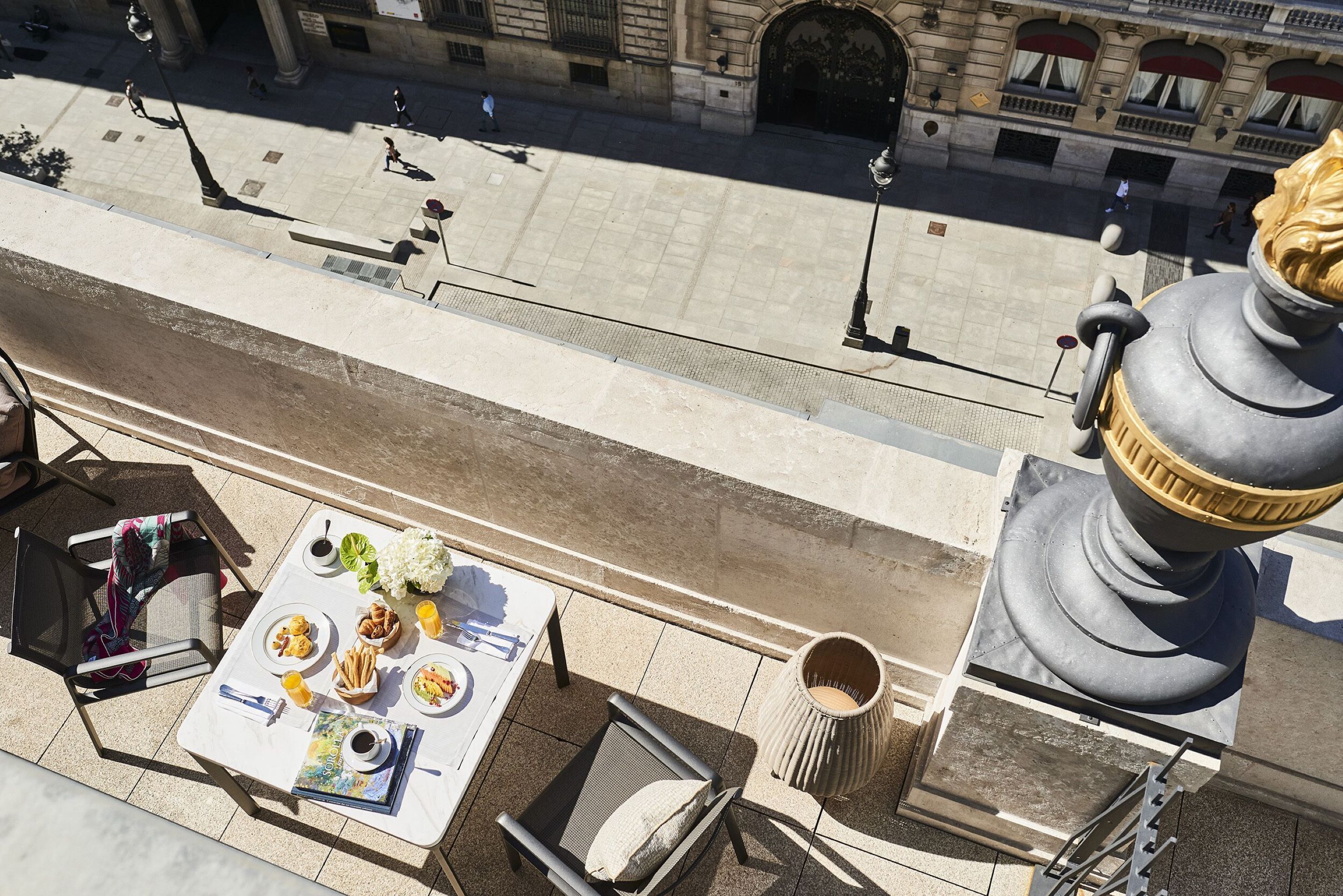 Terraço no telhado com mesa posta para café da manhã, uma cadeira e um vaso decorativo.