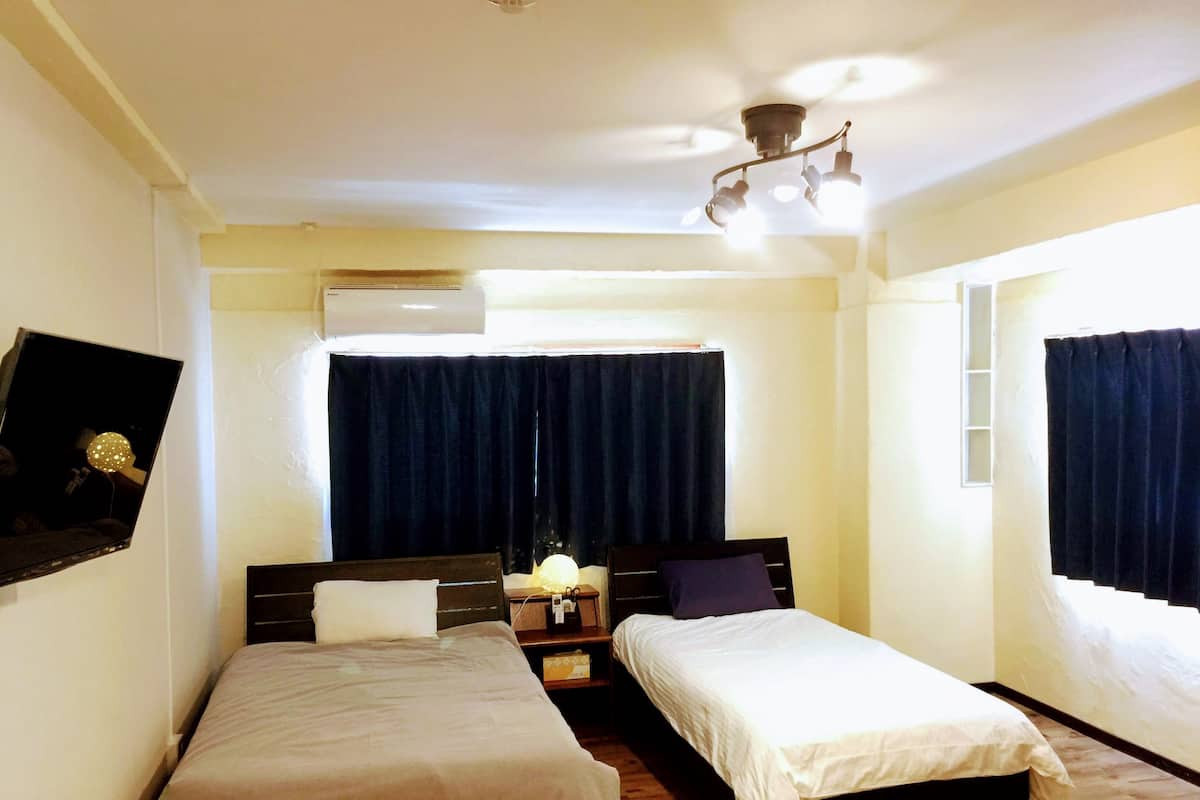 Quarto com duas camas, ventoinha no teto, ar condicionado e janela com cortinas.