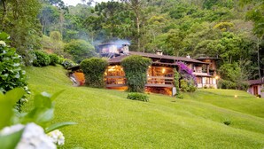 Uma casa de dois andares com varanda, cercada por vegetação exuberante e um gramado bem cuidado.