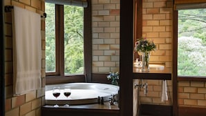 Um banheiro com uma banheira grande, uma janela com vista para o verde e uma pia com um vaso de flores.