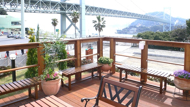 Um deck de madeira com bancos e vasos de plantas, com vista para uma ponte e um corpo de água.