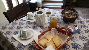 Uma mesa de café da manhã com uma cafeteira, xícaras, um jarro de suco de laranja, uma cesta de pão e uma tigela de cereal.