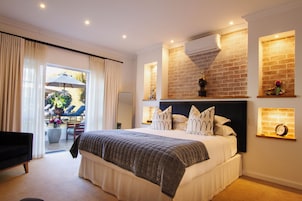 Quarto de hotel com uma cama grande, área de estar com uma poltrona, vista para o exterior e uma parede de tijolos.
