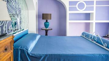 Quarto com cama azul, cómoda de madeira, candeeiro e decoração na parede.