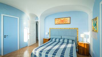 Quarto com cama, duas mesas de cabeceira, porta e corredor.