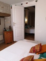 Quarto com cômoda de madeira, porta branca e cama com almofadas estampadas.