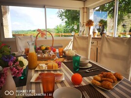 Uma mesa de pequeno-almoço com diversas comidas e bebidas, um vaso com flores e vista para o exterior.