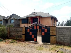 Uma casa de dois andares com portão fechado, varanda visível e entrada por meio de um caminho pavimentado.