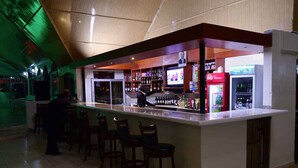 Uma área de bar com balcão, banquetas e uma tela de televisão.