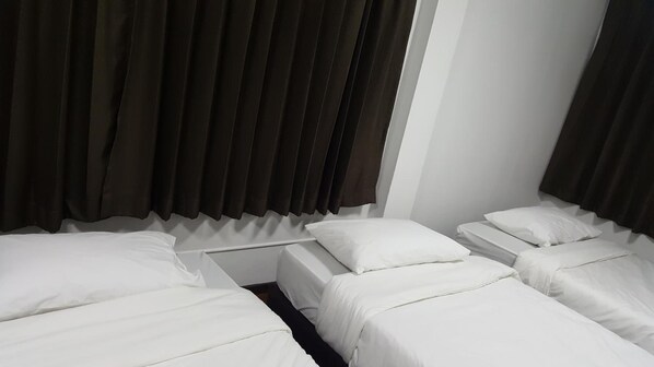 Quarto de hotel com duas camas, cada uma com roupa de cama e almofadas brancas, e cortinas escuras.