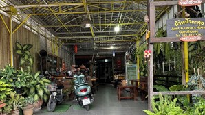 Uma pensão com entrada coberta, plantas em vasos e uma scooter estacionada no interior.