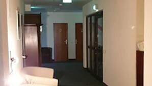 Um corredor com piso coberto por carpete, parede branca e uma porta no final.