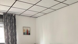 Quarto com cama, escrivaninha, cadeira, planta e janela com cortinas.
