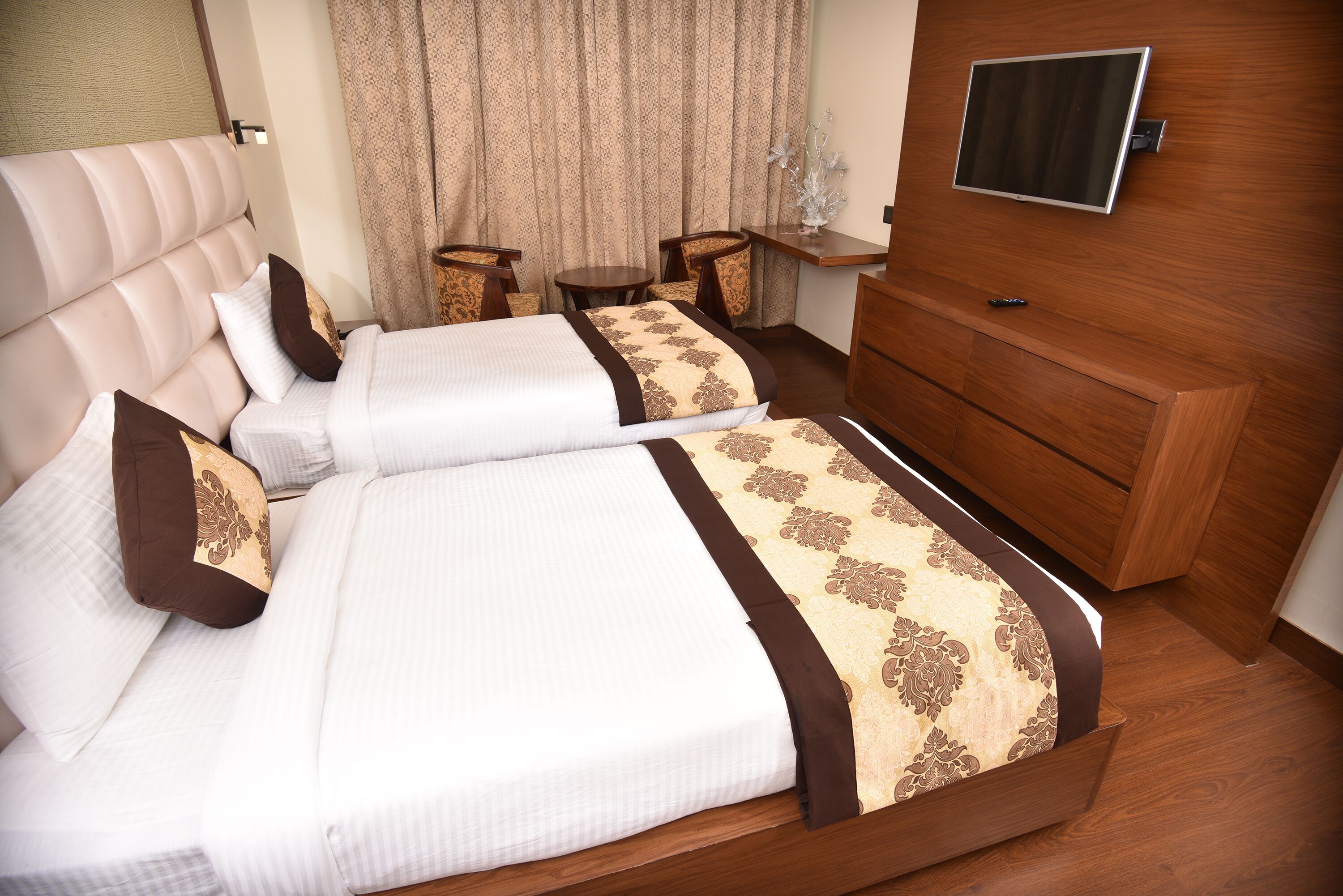 Uma cama de casal com cabeceira, uma mesa de cabeceira, uma pequena mesa com cadeiras, uma TV fixada na parede e um aparador de madeira.