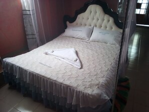 Cama bem arrumada com colcha branca e travesseiros com a etiqueta 'GENNIS PLAZA'.