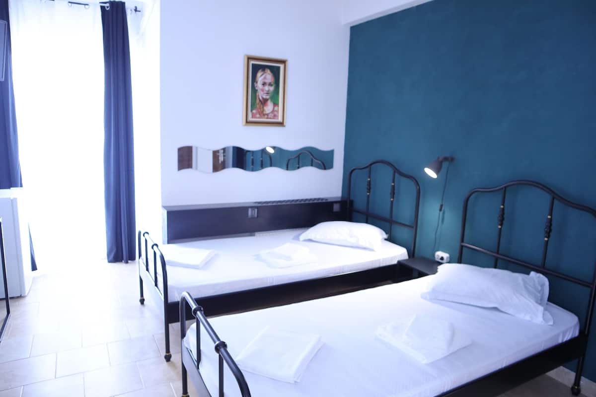 Quarto de hotel com duas camas, um quadro na parede e uma mesa de cabeceira com abajur.