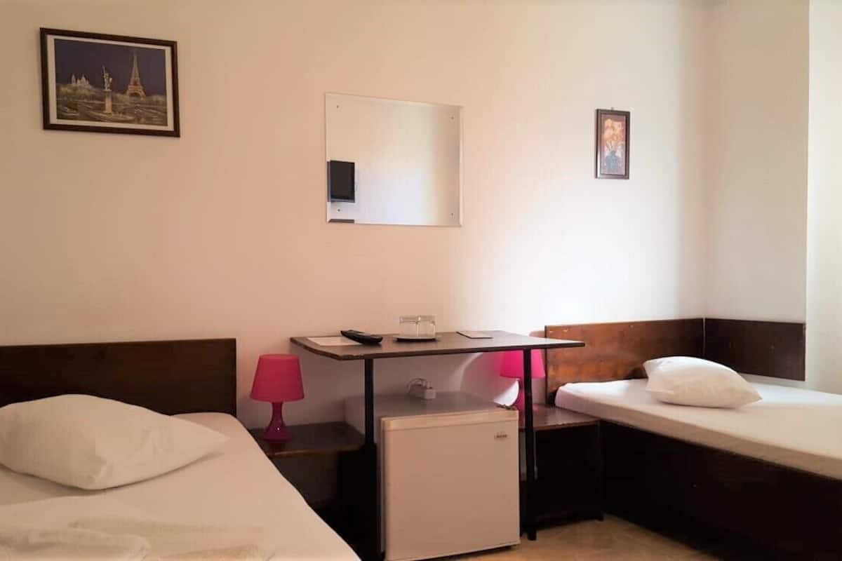 Quarto de hotel com duas camas, uma pequena escrivaninha, um espelho e uma imagem da Torre Eiffel.