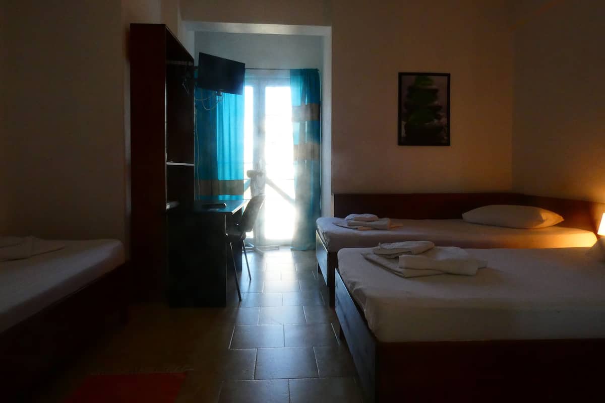 Quarto de hotel com duas camas, uma escrivaninha e uma cadeira. Há uma janela com cortinas e um quadro na parede.