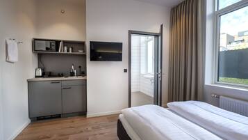 Quarto moderno com cama, cozinha compacta, televisão e janela com cortinas.