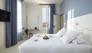 Quarto de hotel com cama, escrivaninha, cadeira, televisão e janela com cortinas.