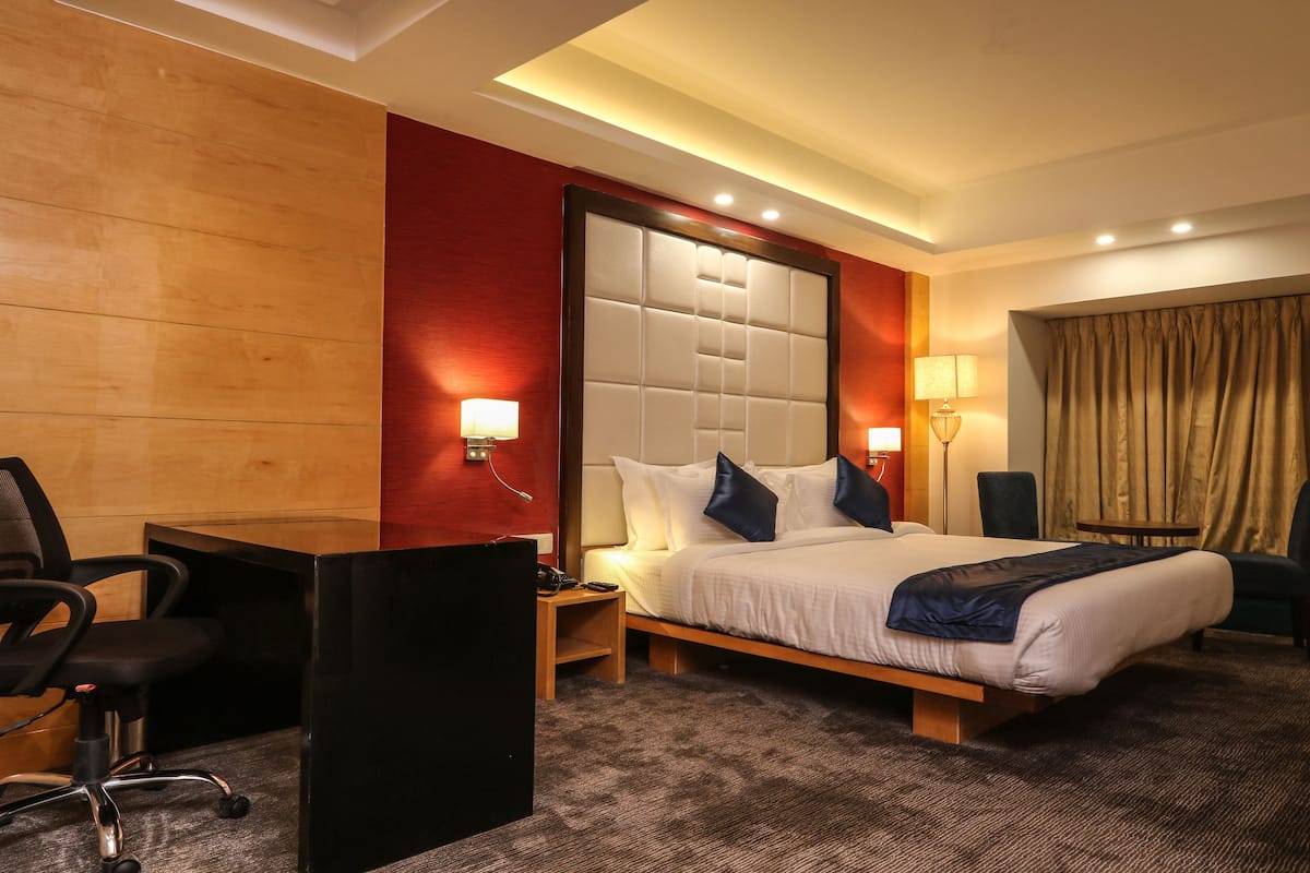 Quarto de hotel com uma cama grande, uma escrivaninha, uma cadeira e uma luminária.