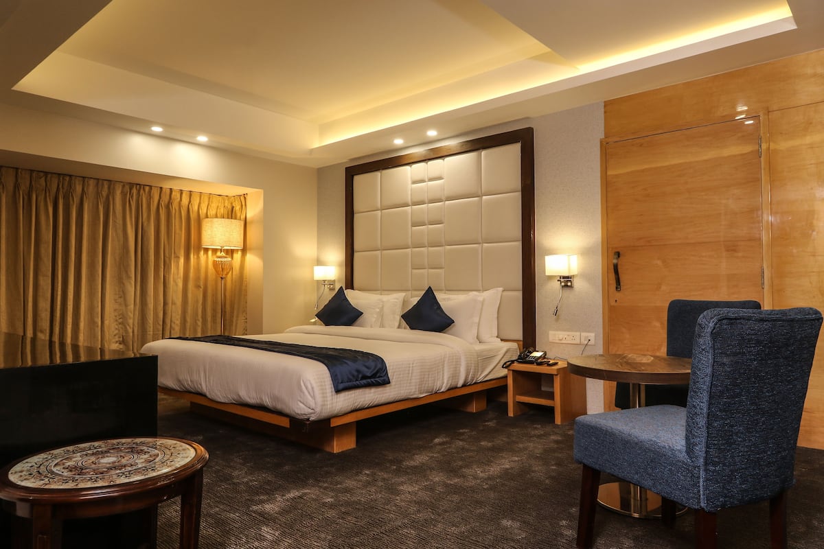 Quarto de hotel com cama, mesas de cabeceira, uma cadeira, uma mesa redonda e um guarda-roupa de madeira grande.