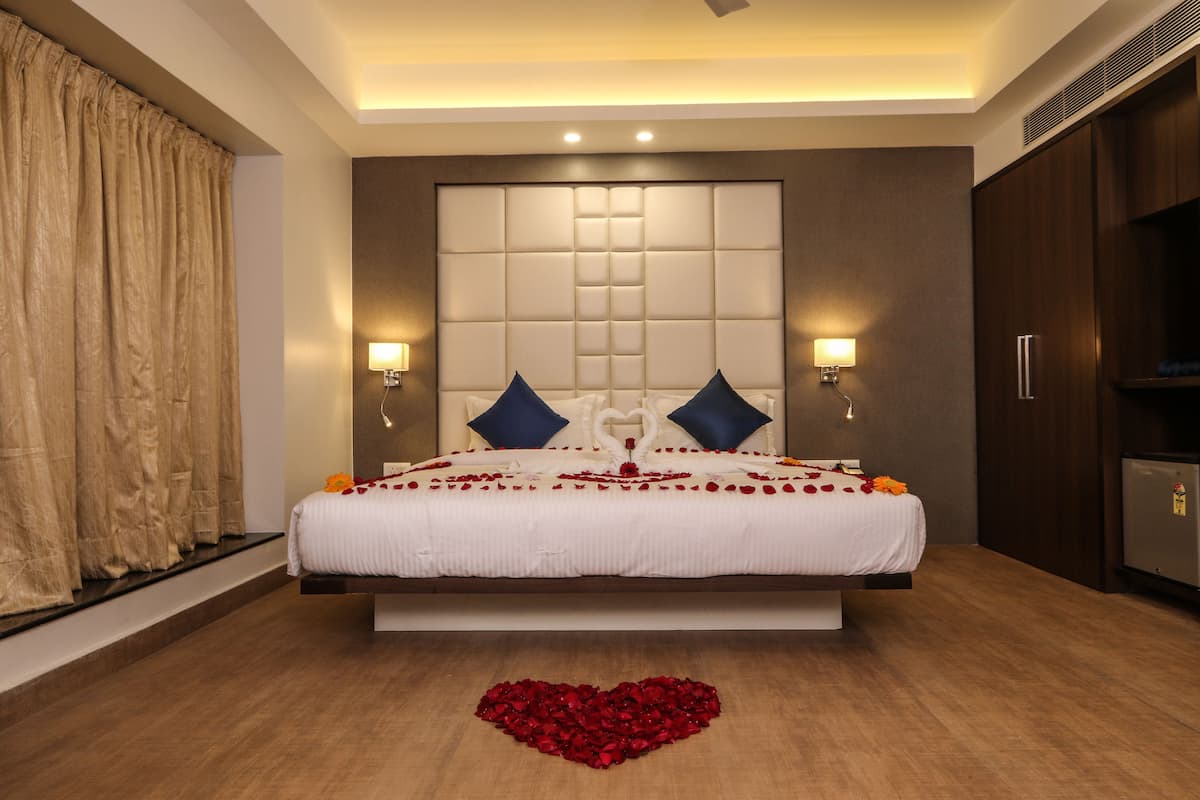 Quarto moderno com uma cama grande, duas luminárias fixadas na parede e um arranjo em forma de coração com flores vermelhas e laranjas no chão.