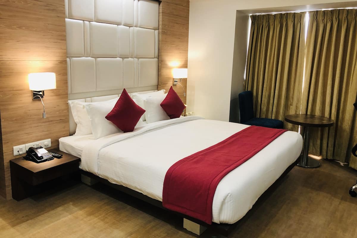 Quarto de hotel com uma cama grande, duas luminárias de cabeceira, um telefone, uma mesinha e uma cadeira.