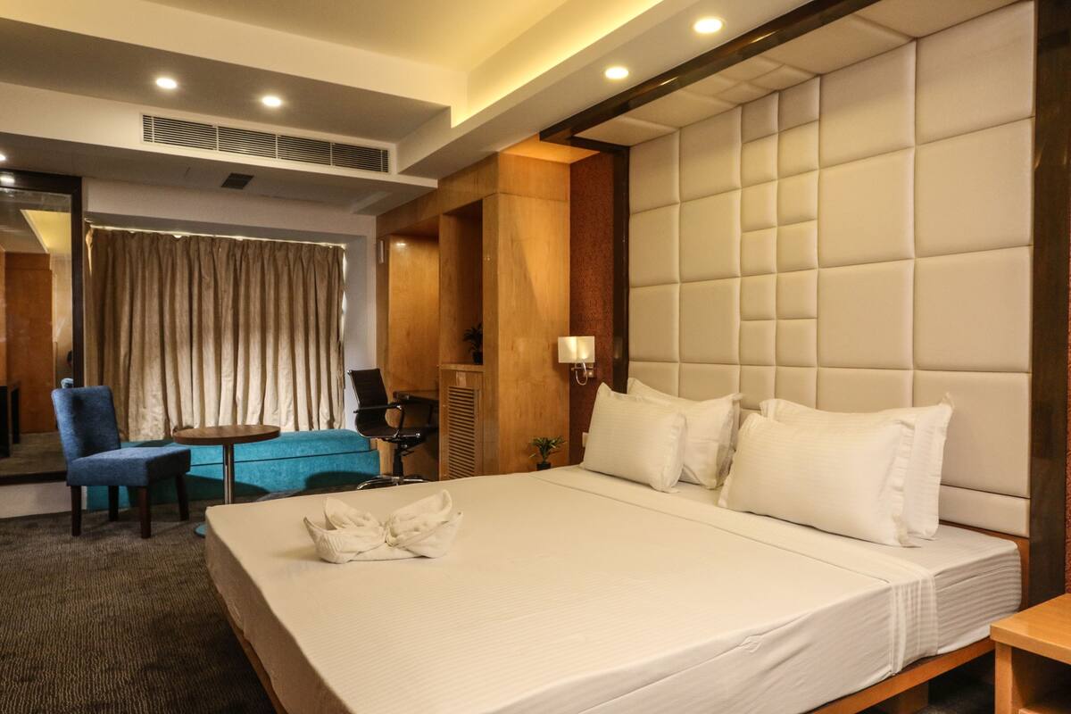 Quarto de hotel com uma cama grande, uma escrivaninha, uma cadeira, uma mesinha e um espelho.