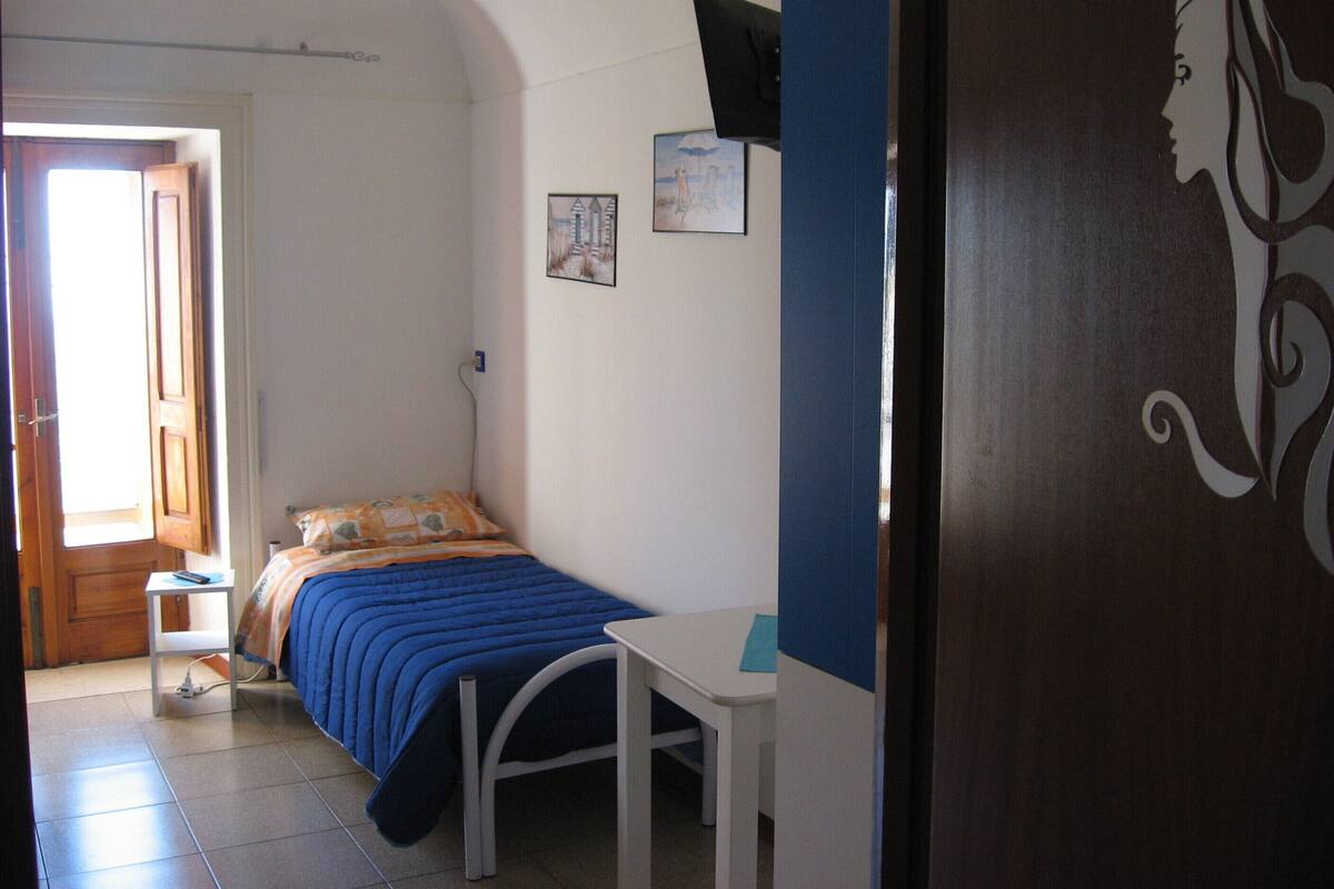 Um quarto com uma cama, uma escrivaninha e uma porta.