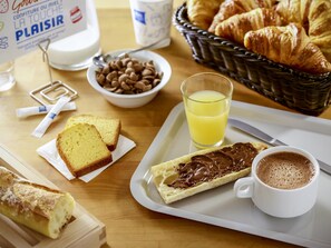 Uma bandeja de café da manhã com croissants, um sanduíche, um copo de suco de laranja, uma xícara de café e uma tigela de gotas de chocolate.