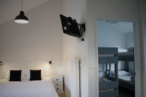 Quarto com uma cama de solteiro, mesa de cabeceira, luminária e televisão fixada na parede.